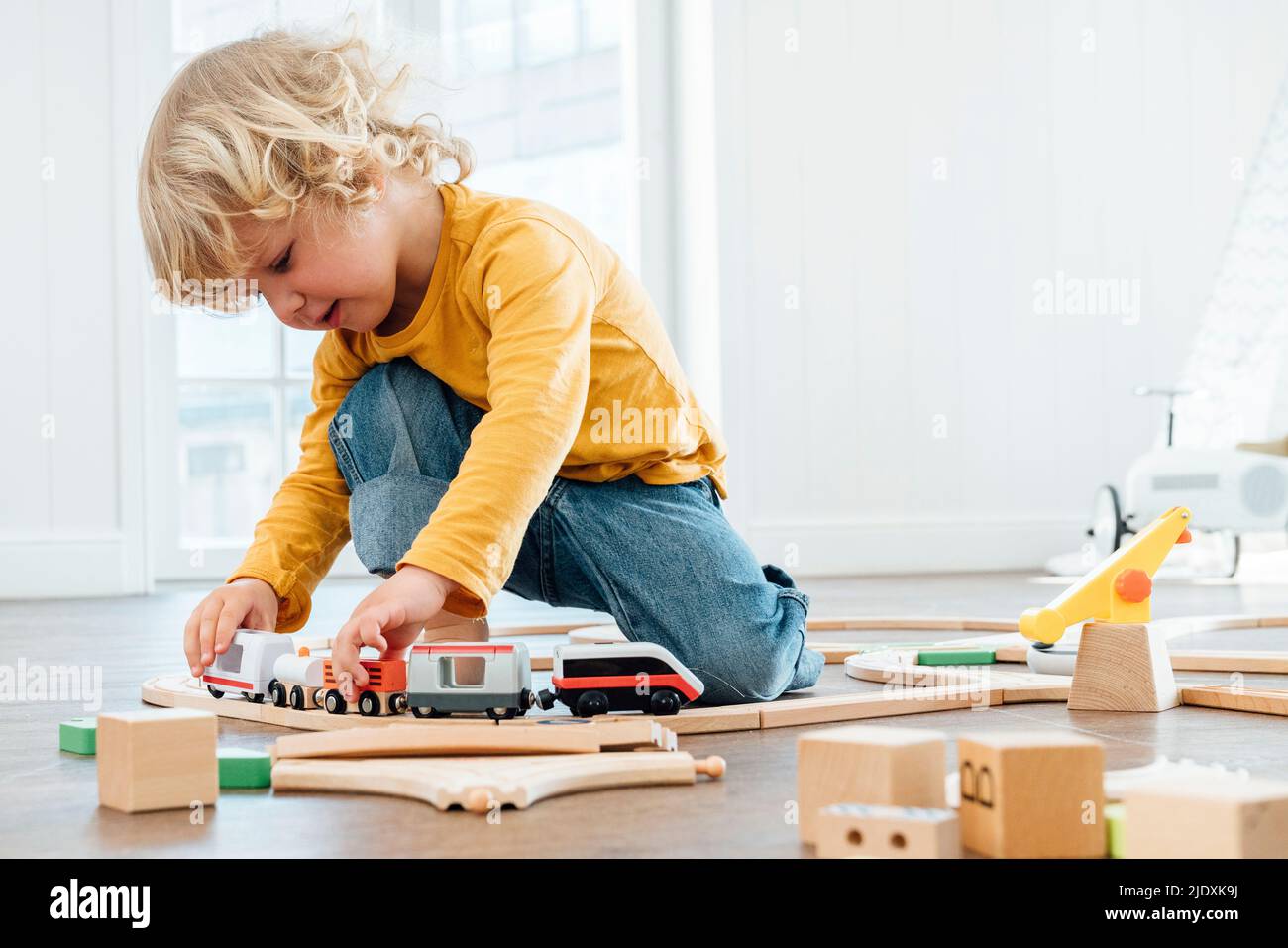 Cute boy with blond hair playing with toy train set at home Stock Photo ...