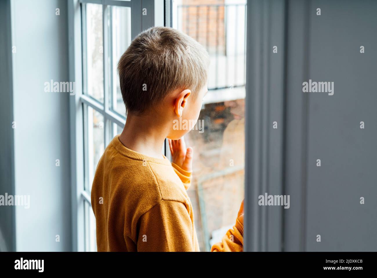Boy looking through window at home Stock Photo - Alamy