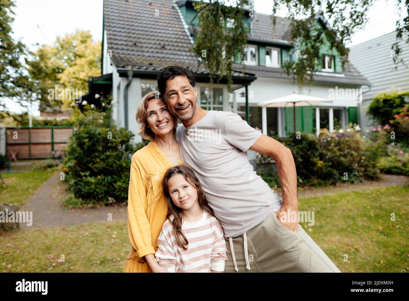 Happy parents with daughter standing in front of house Stock Photo - Alamy