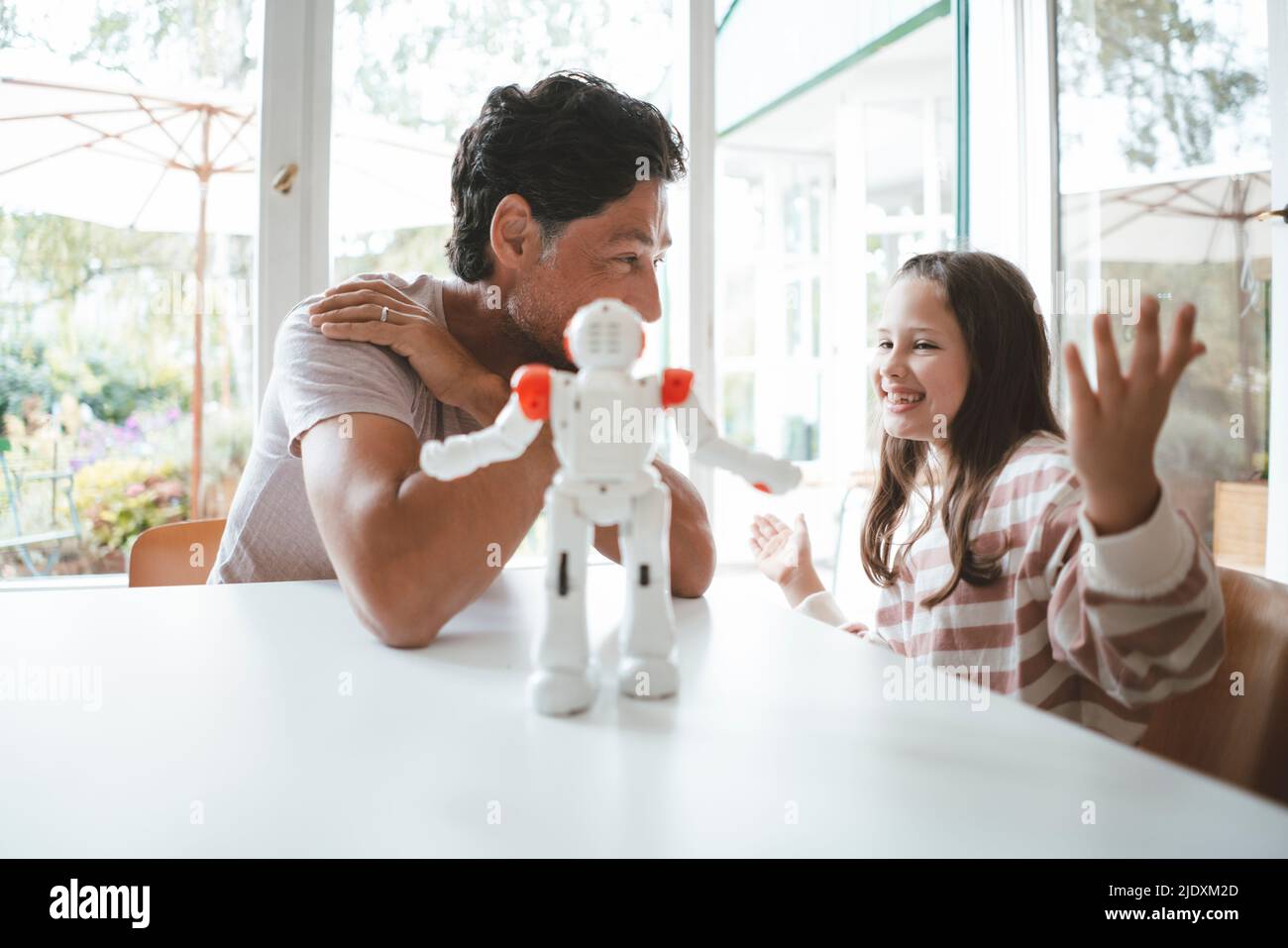 Happy daughter and father sitting with toy robot on table at home Stock ...