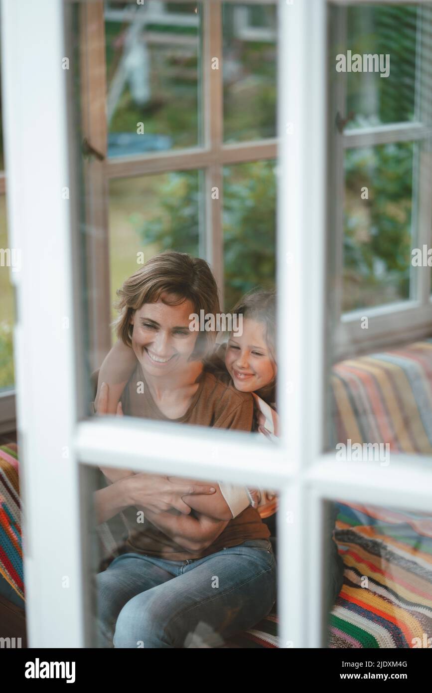 Happy woman with daughter sitting on sofa seen through window Stock Photo - Alamy
