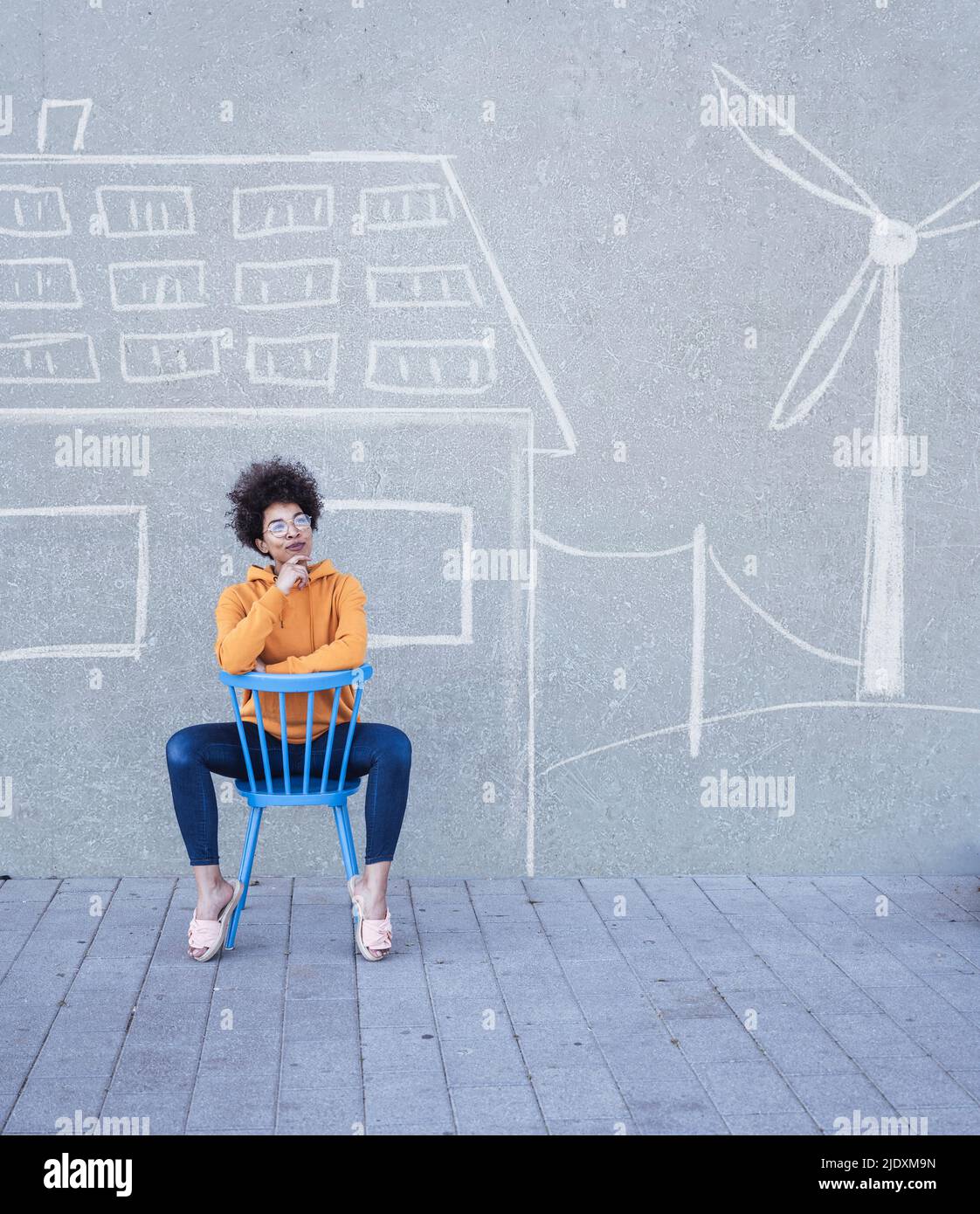 Thoughtful woman sitting on chair in front of wall with painted wind ...