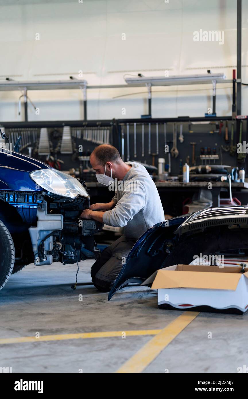 Auto mechanic kneeling and repairing car in garage Stock Photo - Alamy