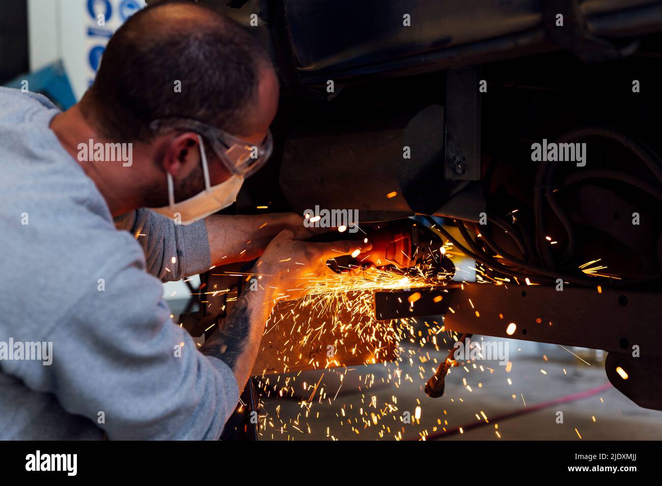 Mechanic wearing protective face mask cutting metal of car in auto ...