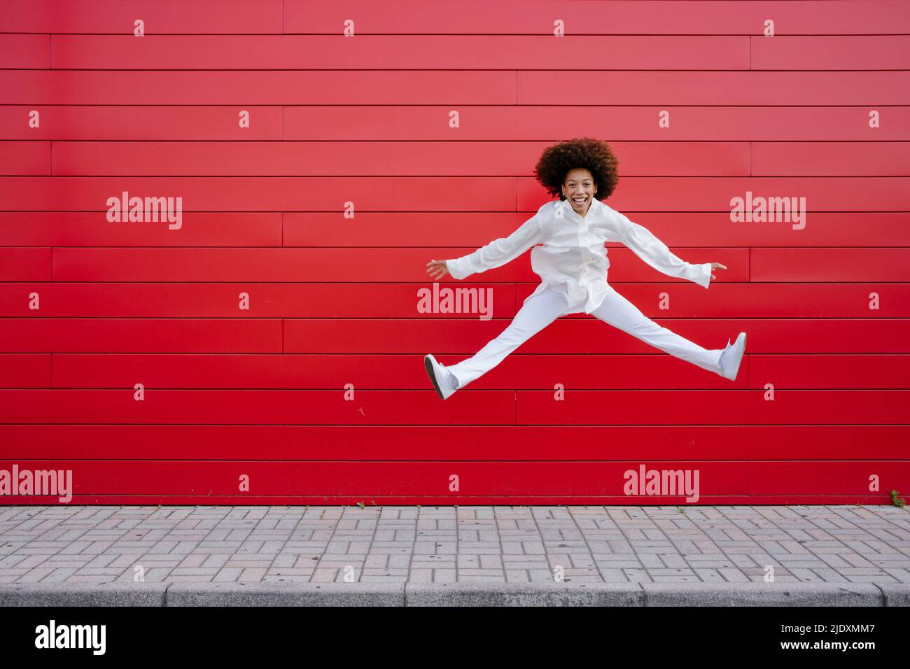 Cheerful young woman doing splits in front of red wall Stock Photo - Alamy