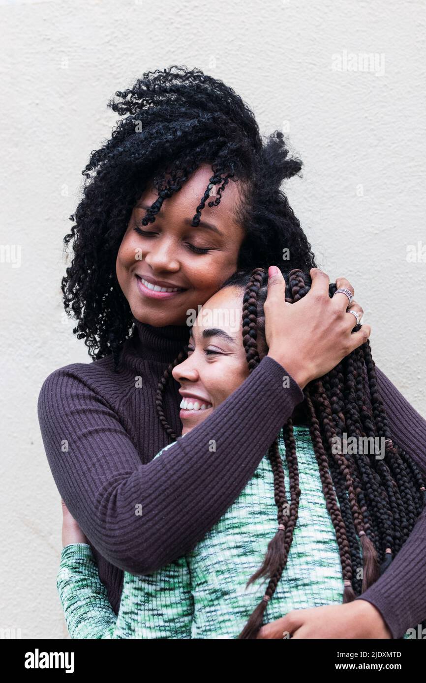 Happy woman hugging friend standing in front of wall Stock Photo - Alamy