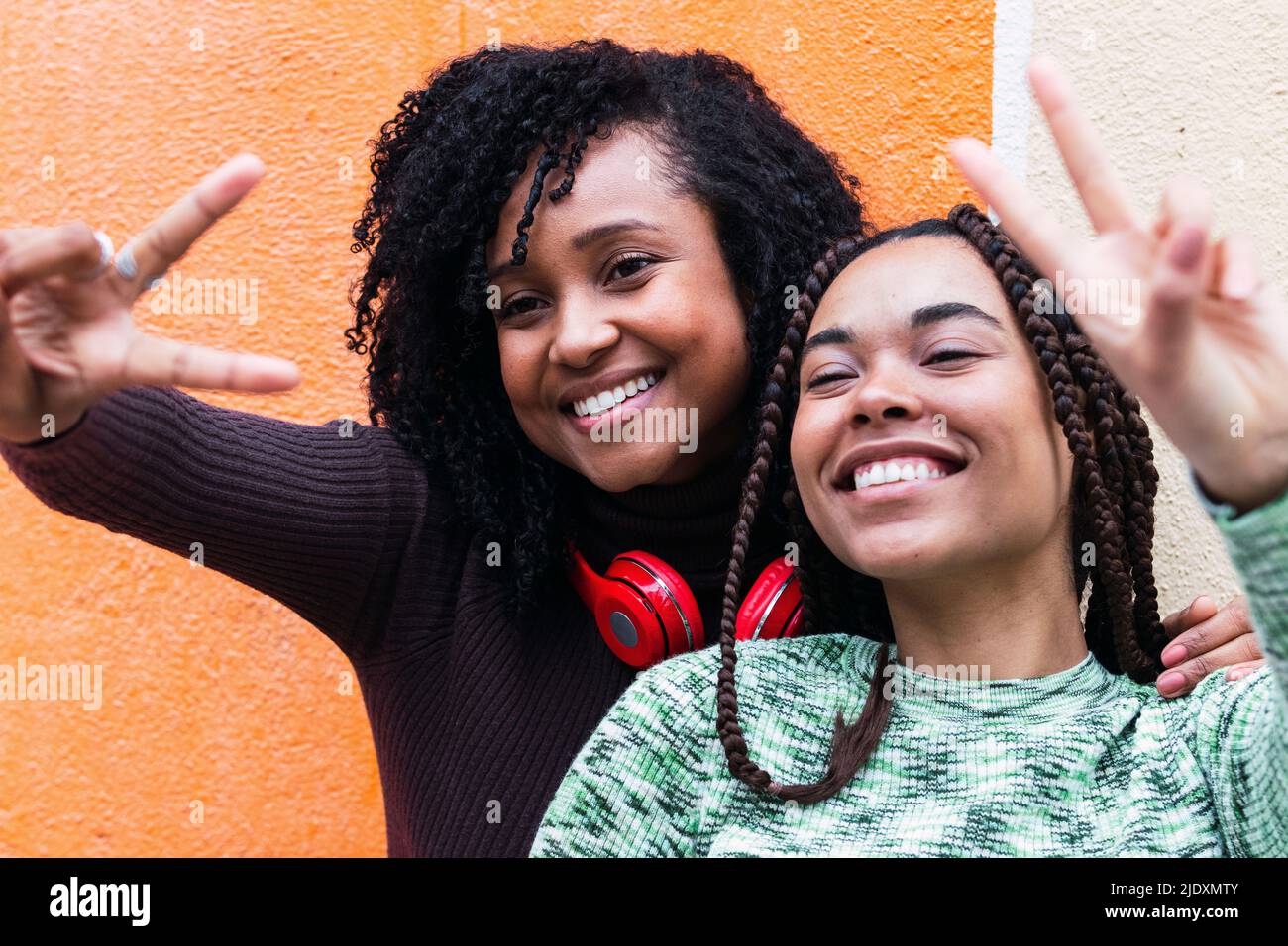 Happy friends gesturing peace sign in front of wall Stock Photo - Alamy