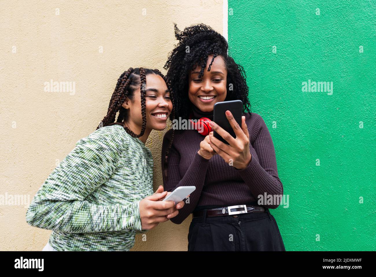 Happy multiracial friends with mobile phones standing in front of wall ...