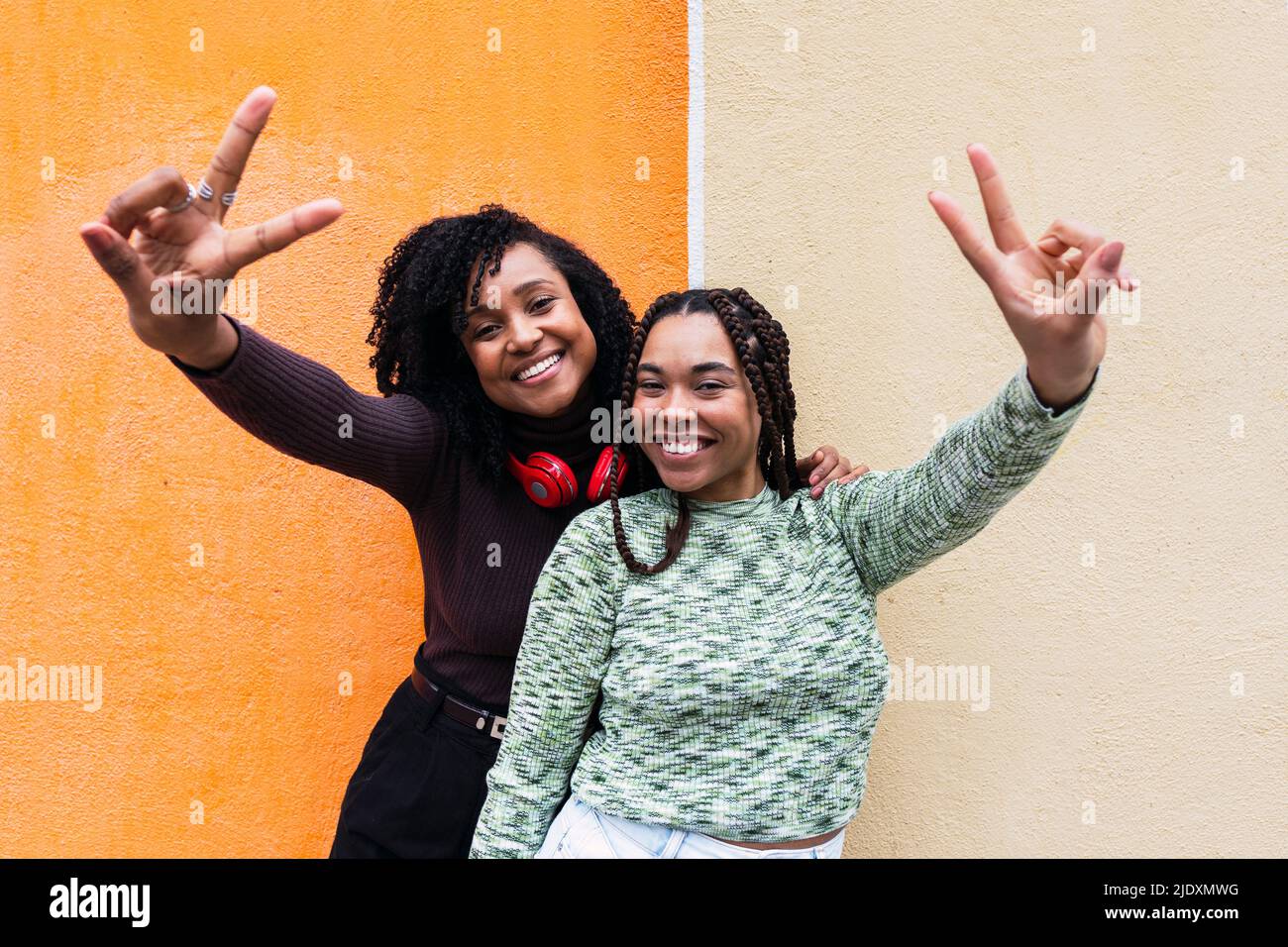 Happy friends gesturing peace sign in front of wall Stock Photo - Alamy