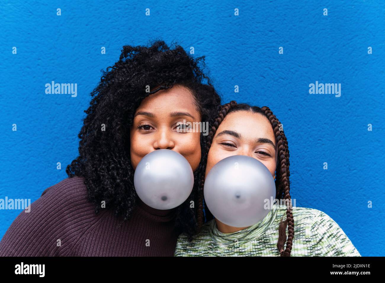 Friends blowing gum bubbles in front of blue wall Stock Photo - Alamy