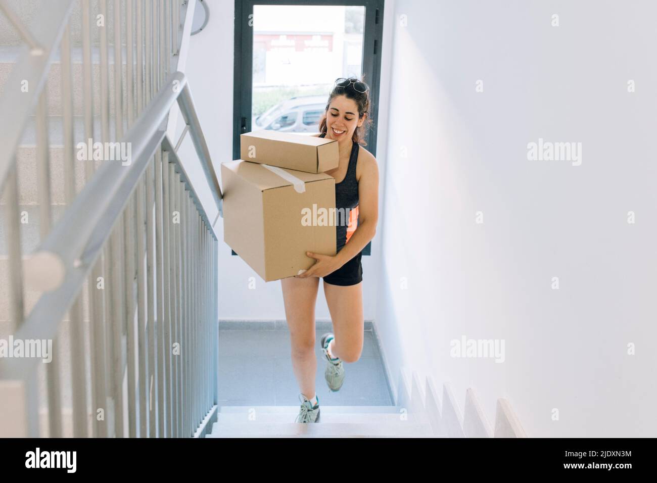Happy woman carrying cardboard boxes moving up on steps Stock Photo - Alamy