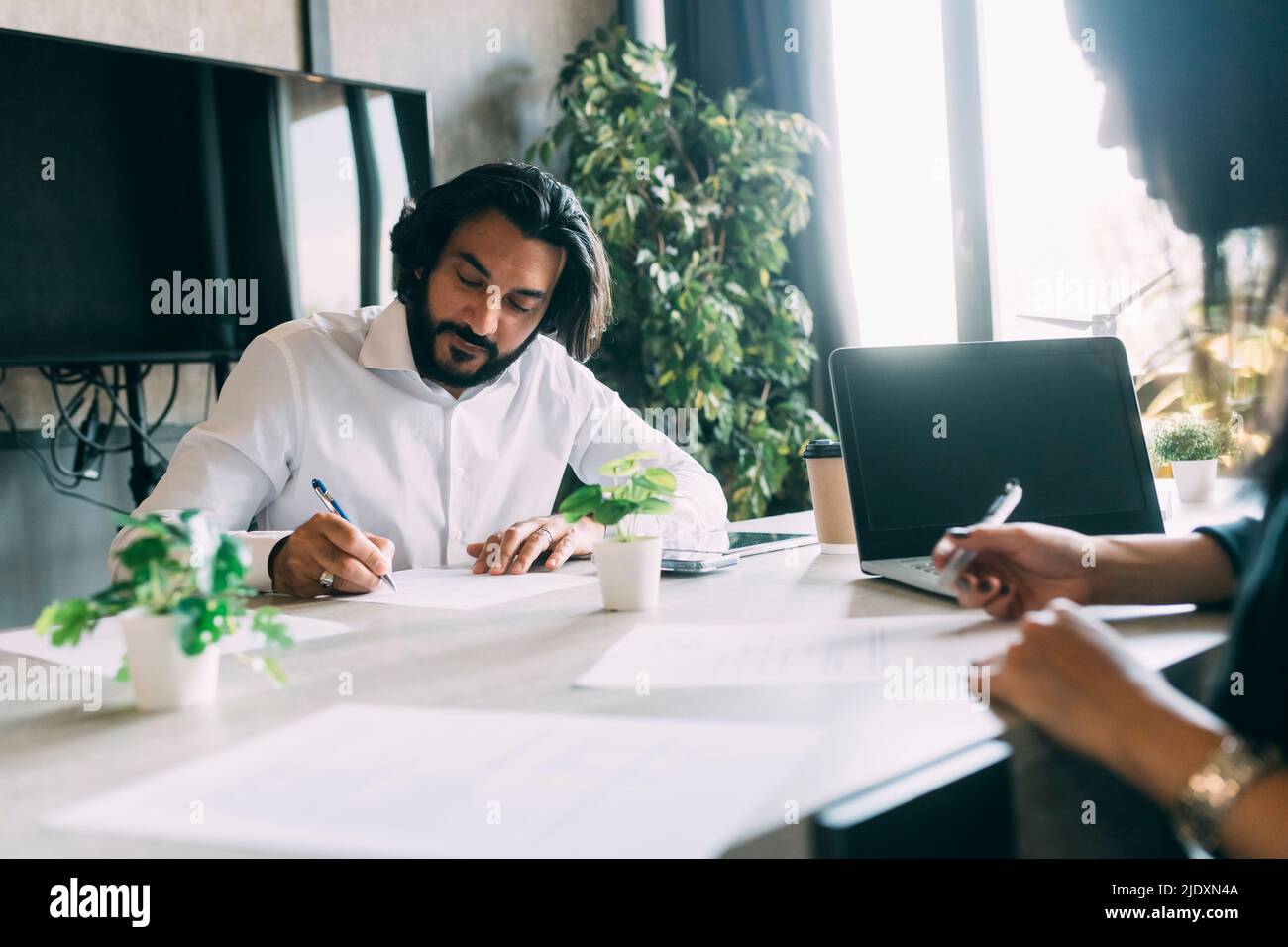 Multiracial colleagues writing on paper document at desk in workplace ...