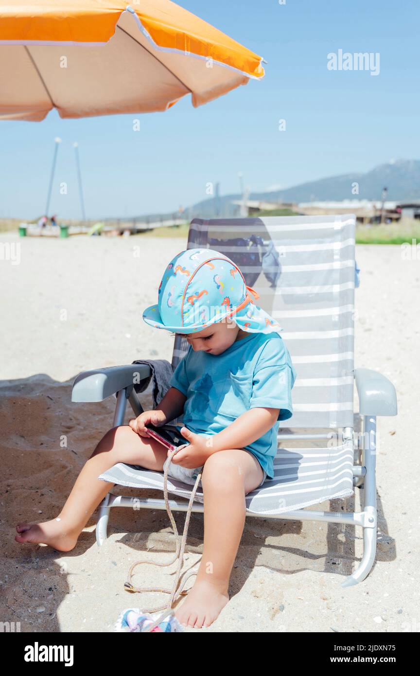 Boy with smart phone sitting on deck chair at beach Stock Photo - Alamy