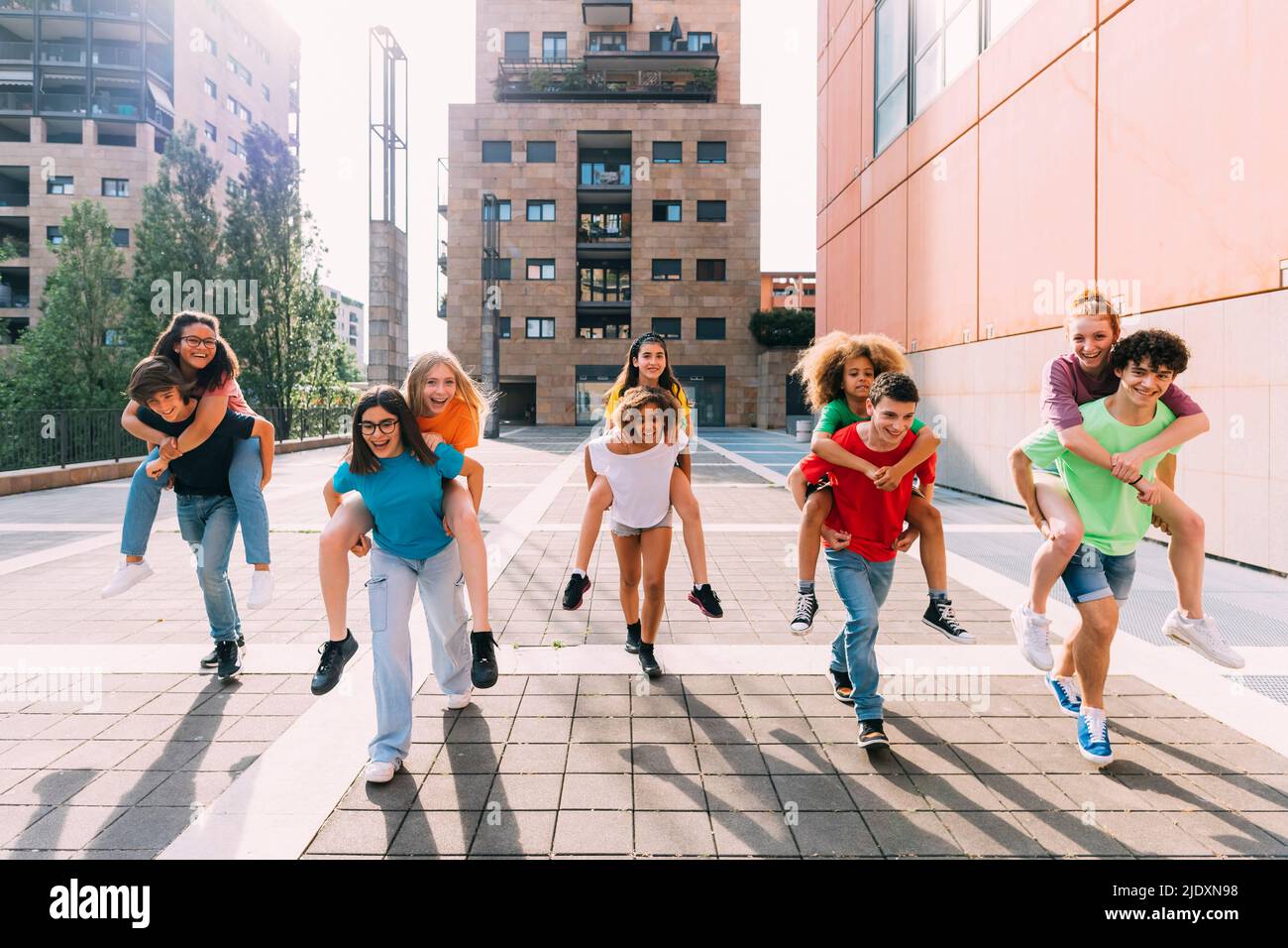Cheerful girls and boys giving piggyback ride to friends on sunny day ...