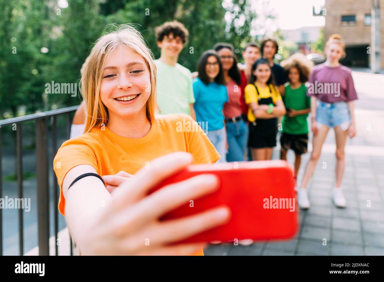 Happy blond girl taking selfie through mobile phone with friends Stock ...
