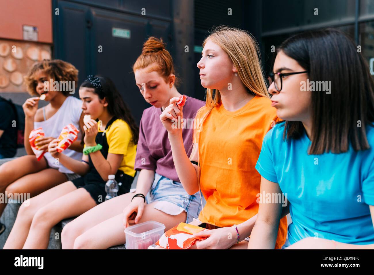 Girls sitting together eating snacks Stock Photo - Alamy