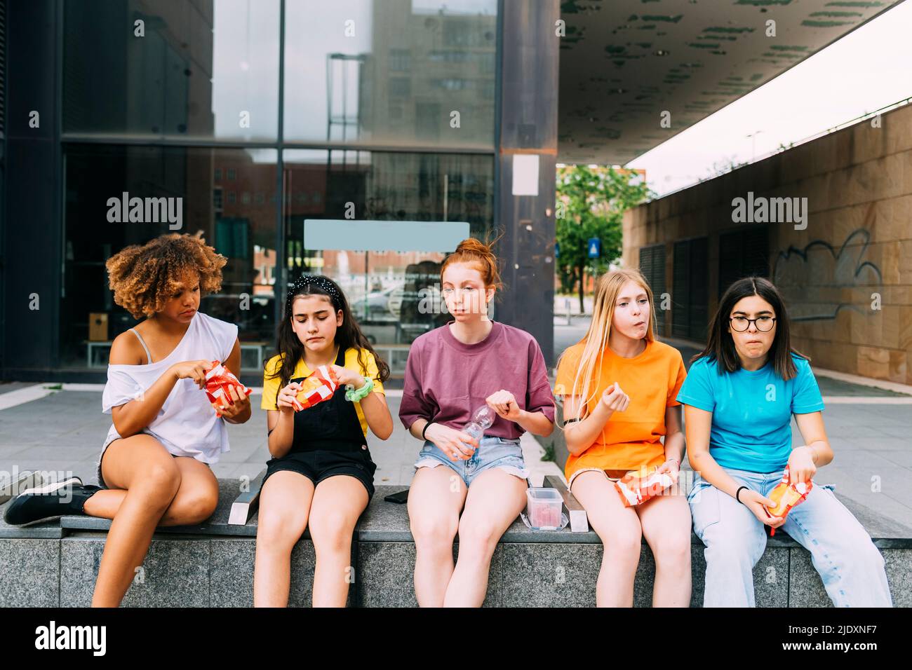 Multiracial friends eating snacks sitting in front of building Stock ...