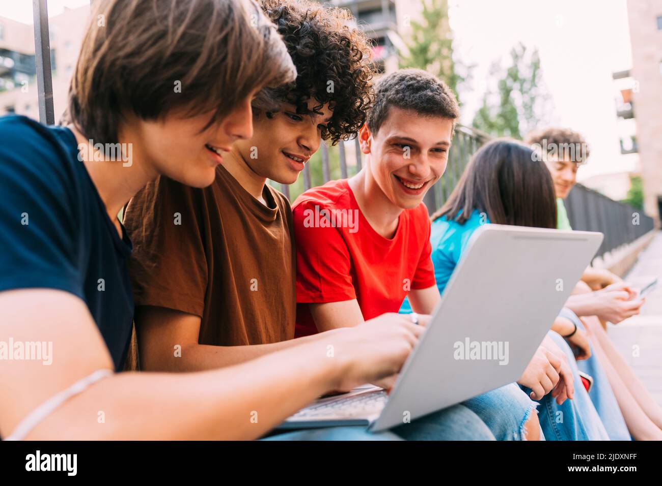Happy boys sharing laptop sitting by friends Stock Photo - Alamy