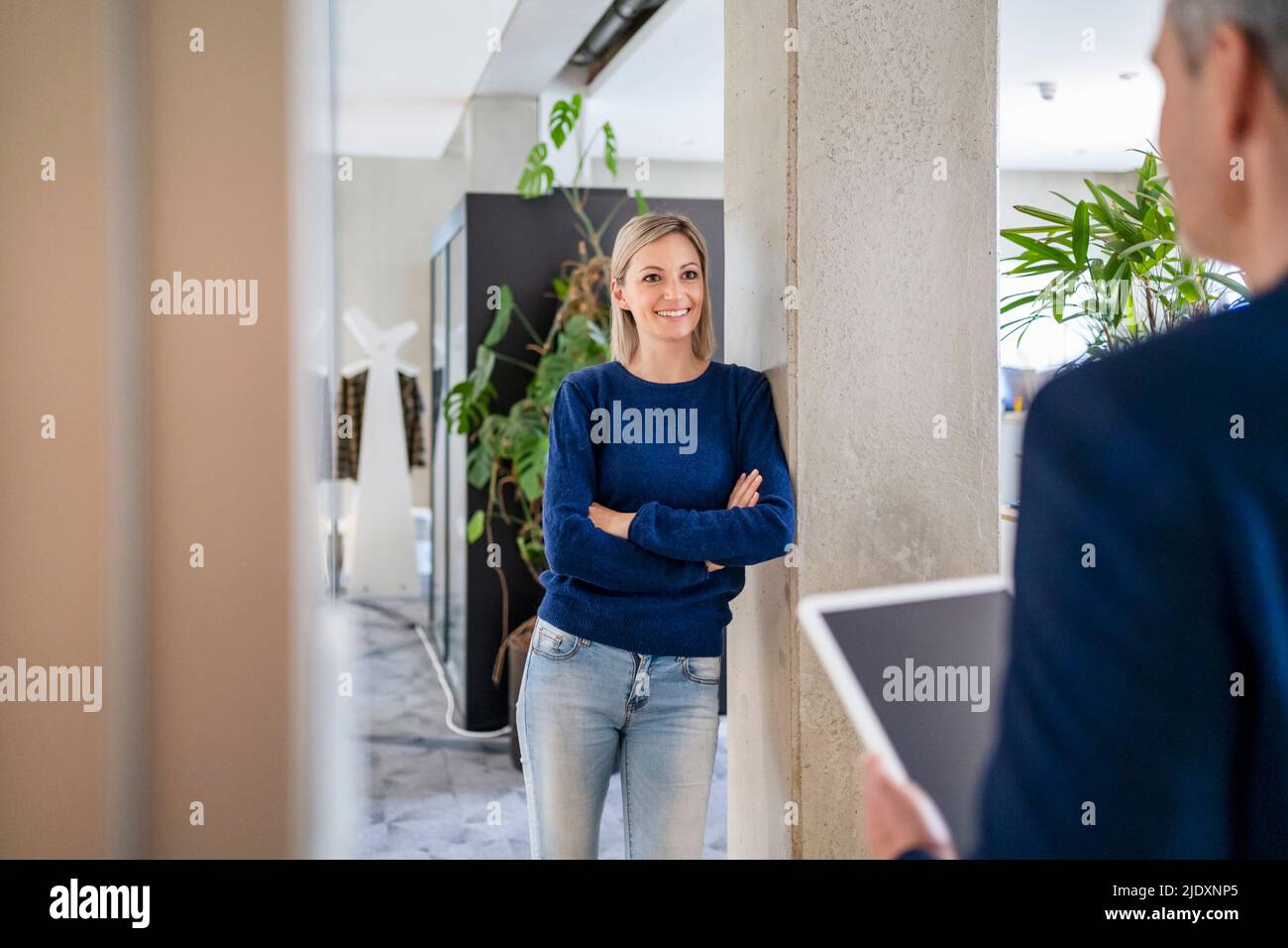 Smiling businesswoman leaning against column in office looking at ...