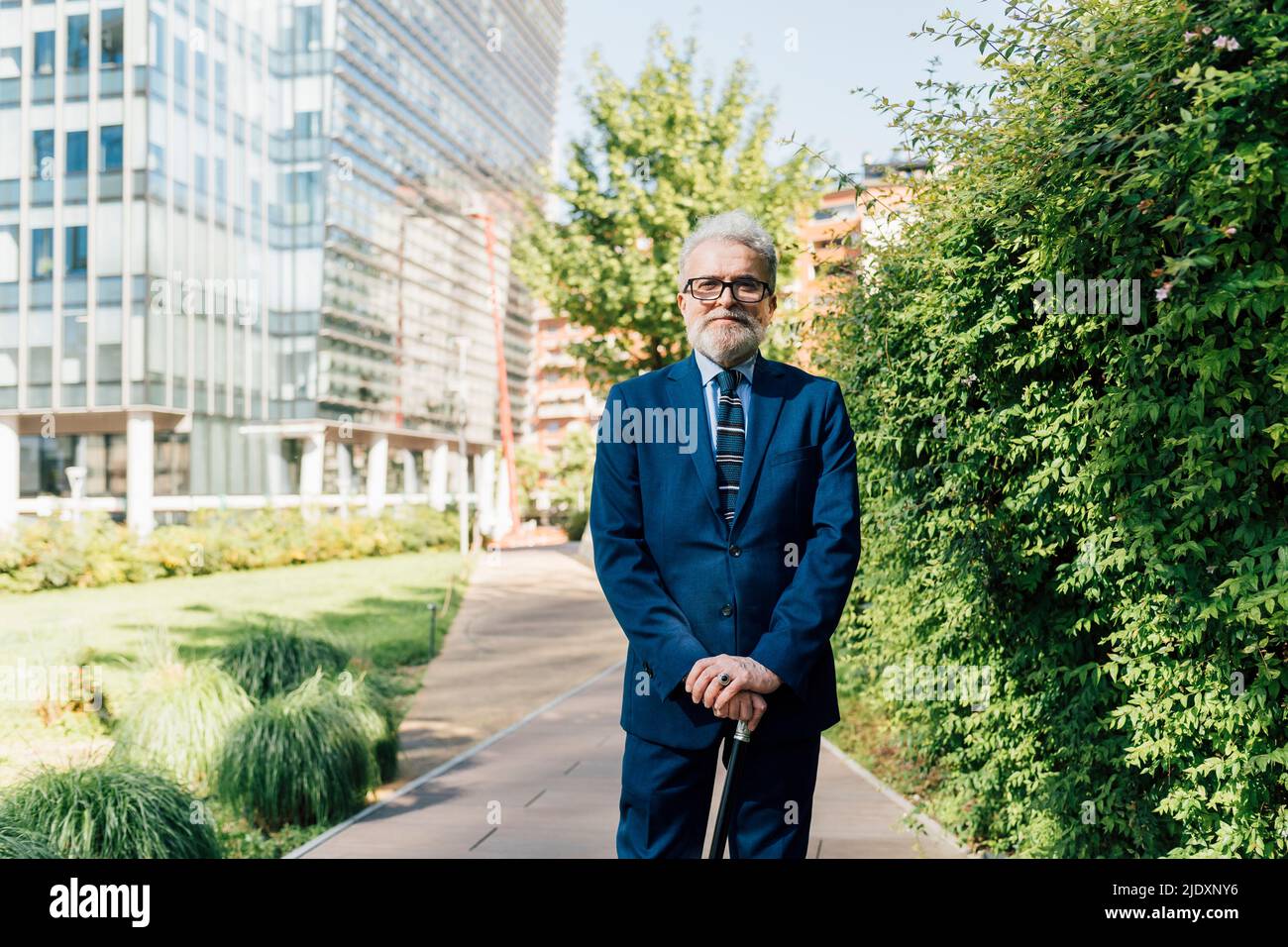 Happy senior businessman standing with cane at office park Stock Photo ...
