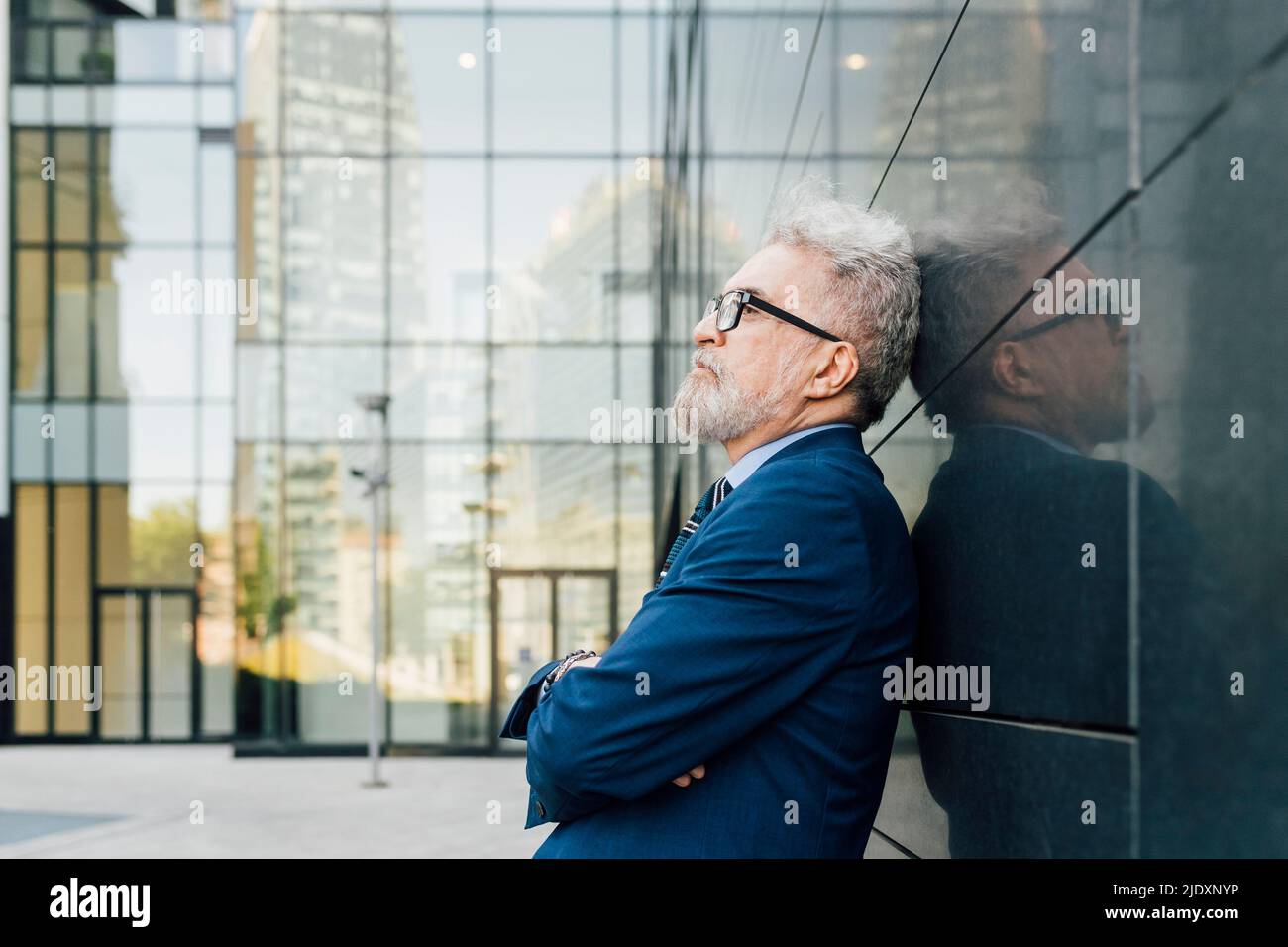 Thoughtful senior businessman leaning on wall outside office building ...