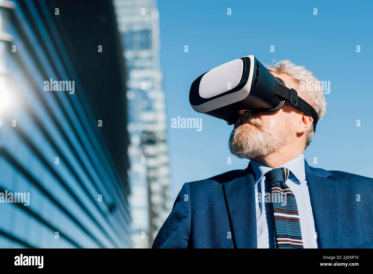 Senior businessman wearing virtual reality simulator outside office ...