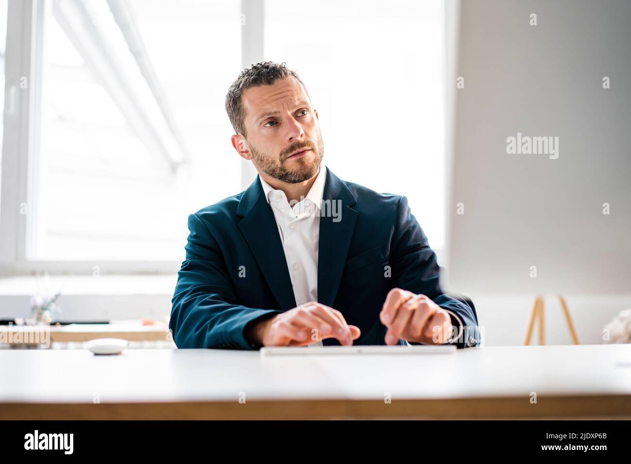Contemplated businessman with tablet PC sitting at desk in office Stock ...