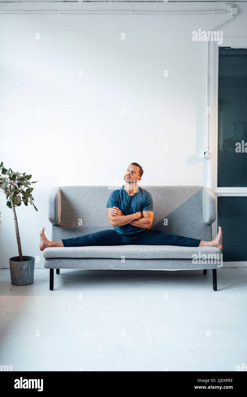 Thoughtful man stretching legs sitting with arms crossed on sofa at ...