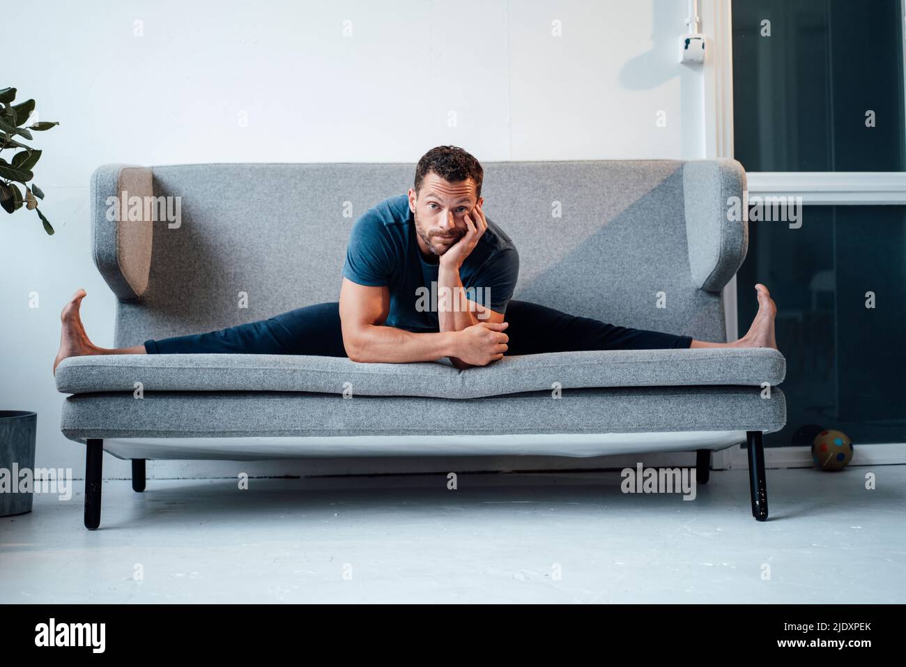 Man with legs apart sitting on sofa at home Stock Photo - Alamy
