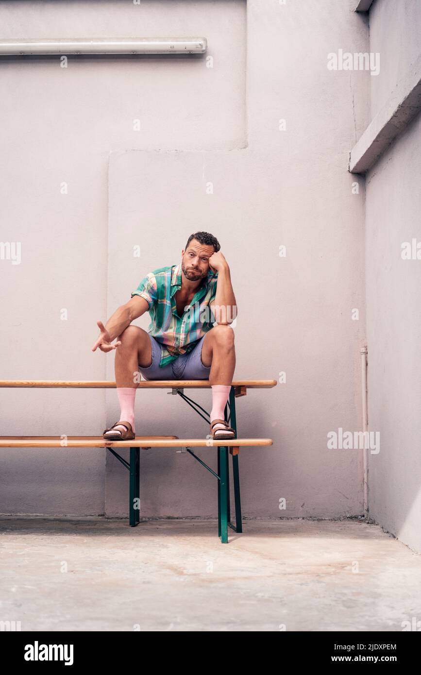 Confused man gesturing sitting on bench in front of wall Stock Photo ...