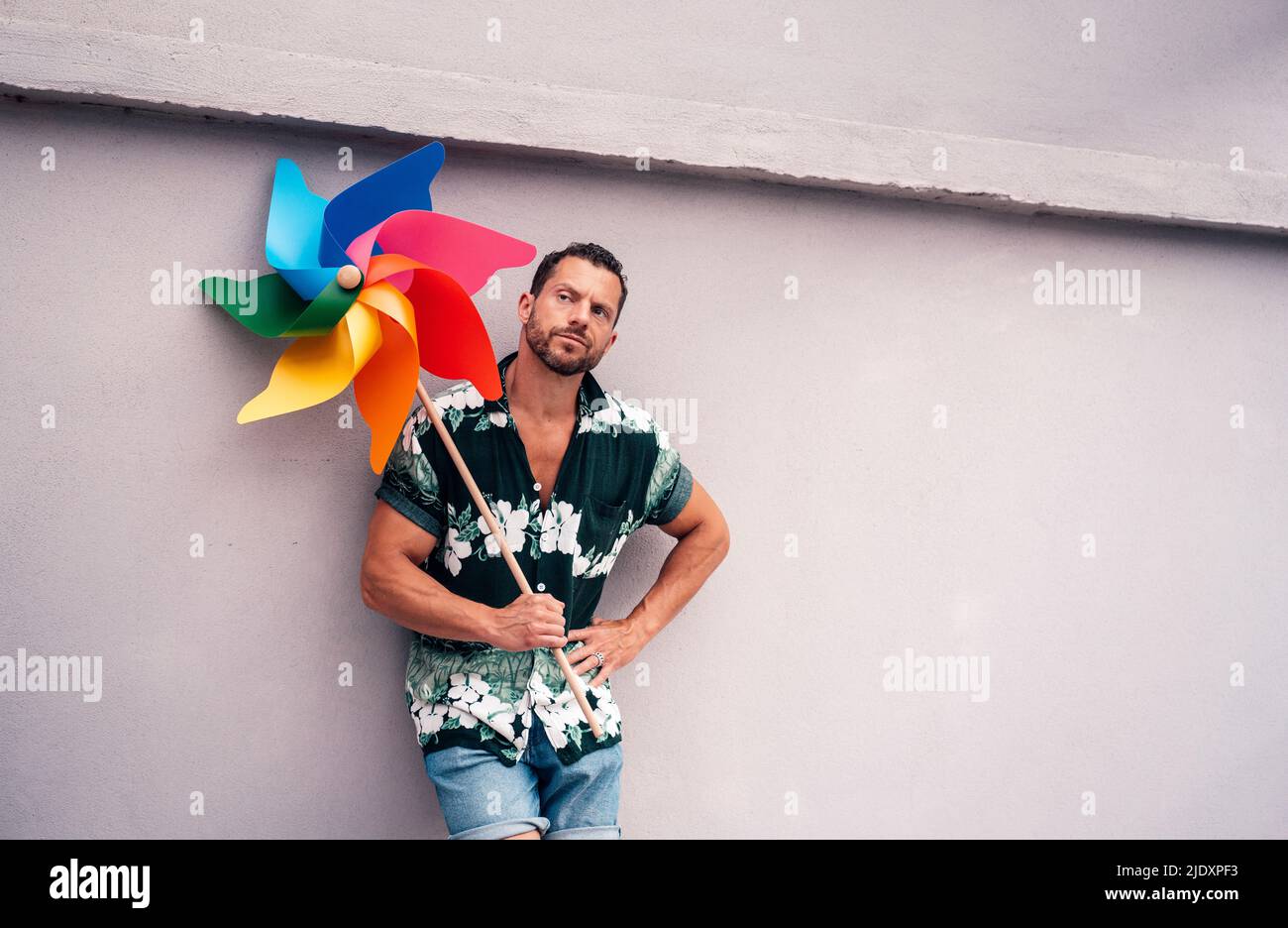 Thoughtful man with hand on hip holding pinwheel toy leaning on ...