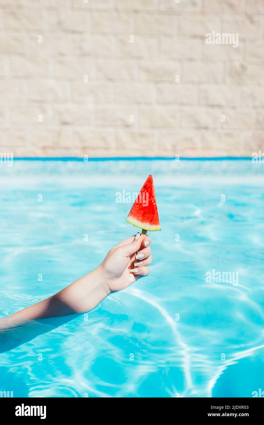 Hand of woman holding watermelon slice with popsicle stick in swimming ...