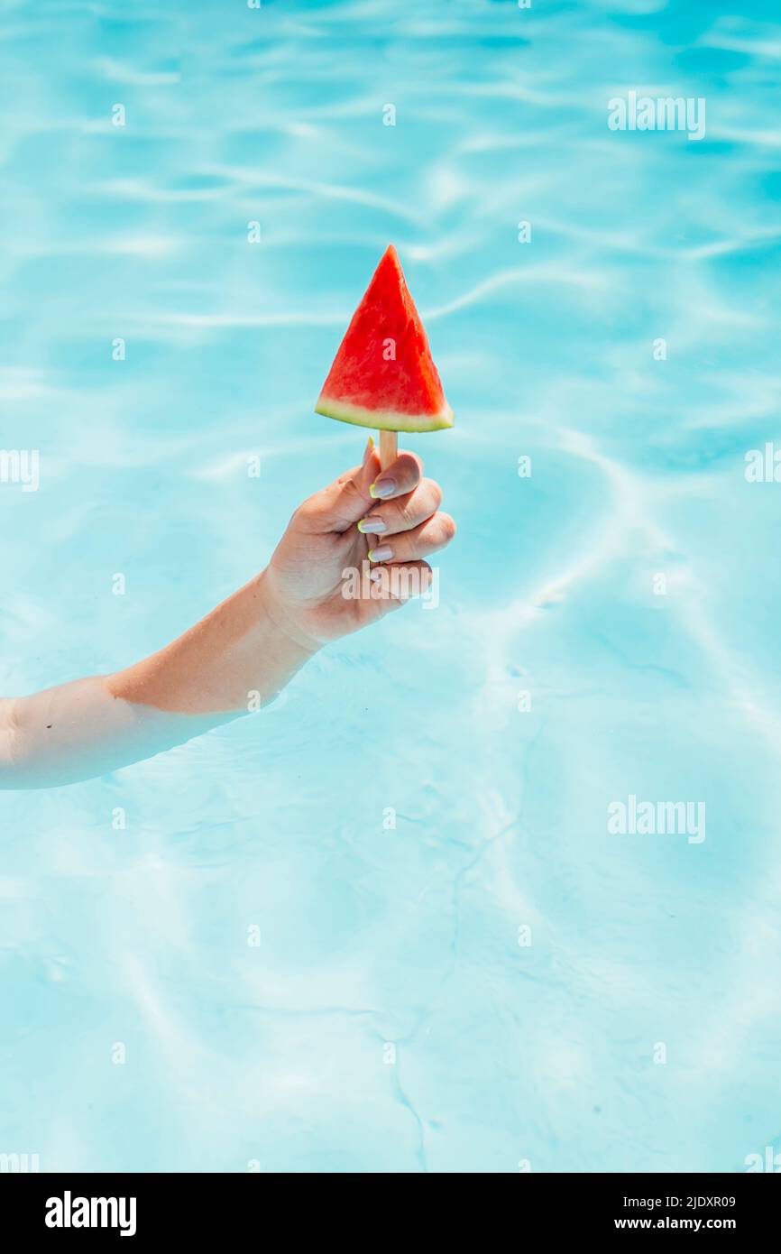 Hand of young woman holding watermelon slice with popsicle stick in ...