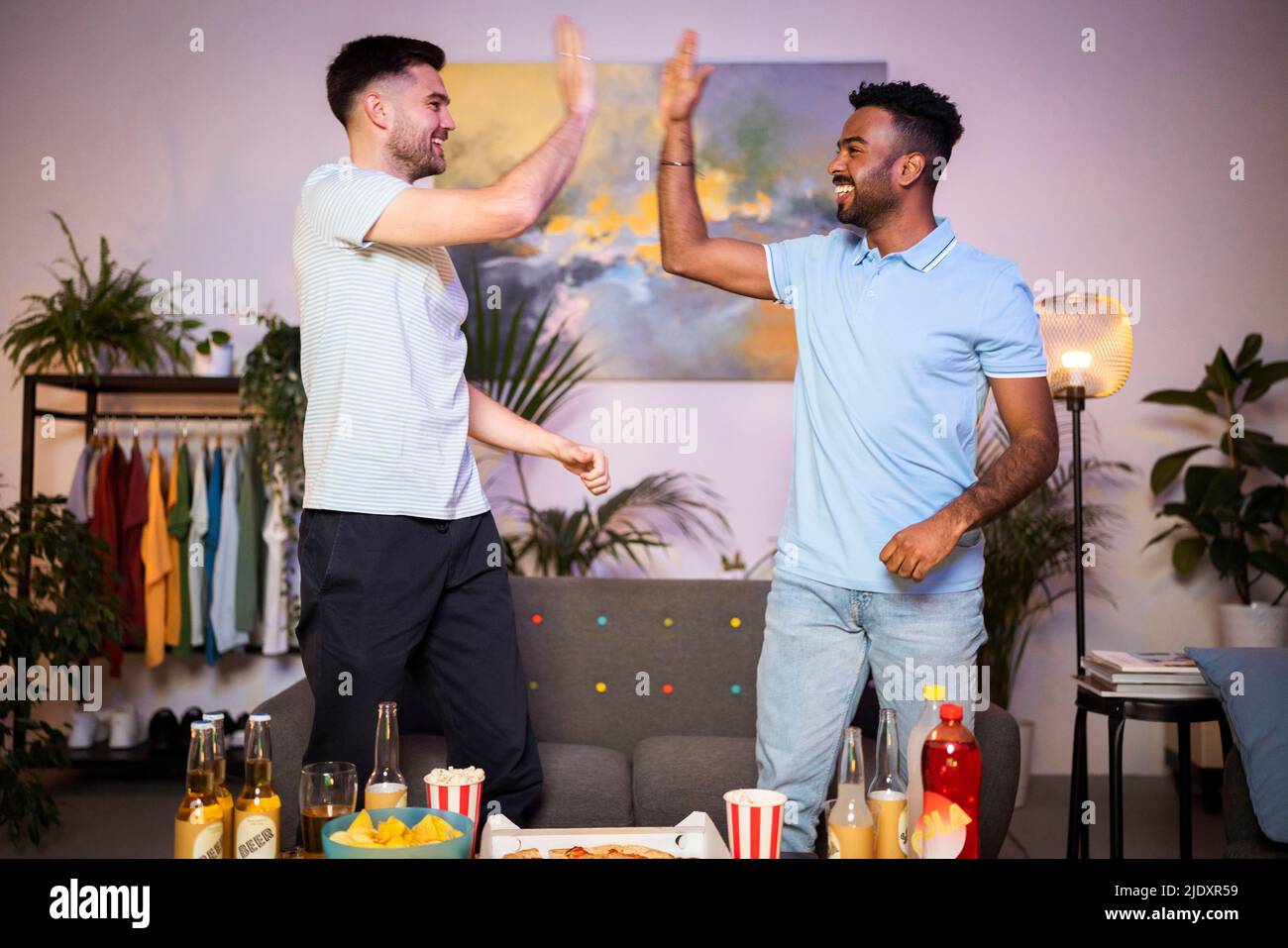 Happy young men giving high-five to each other standing in living room ...