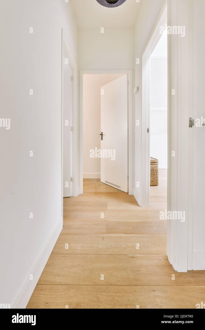 Narrow corridor with white walls and doors leading to room with parquet ...