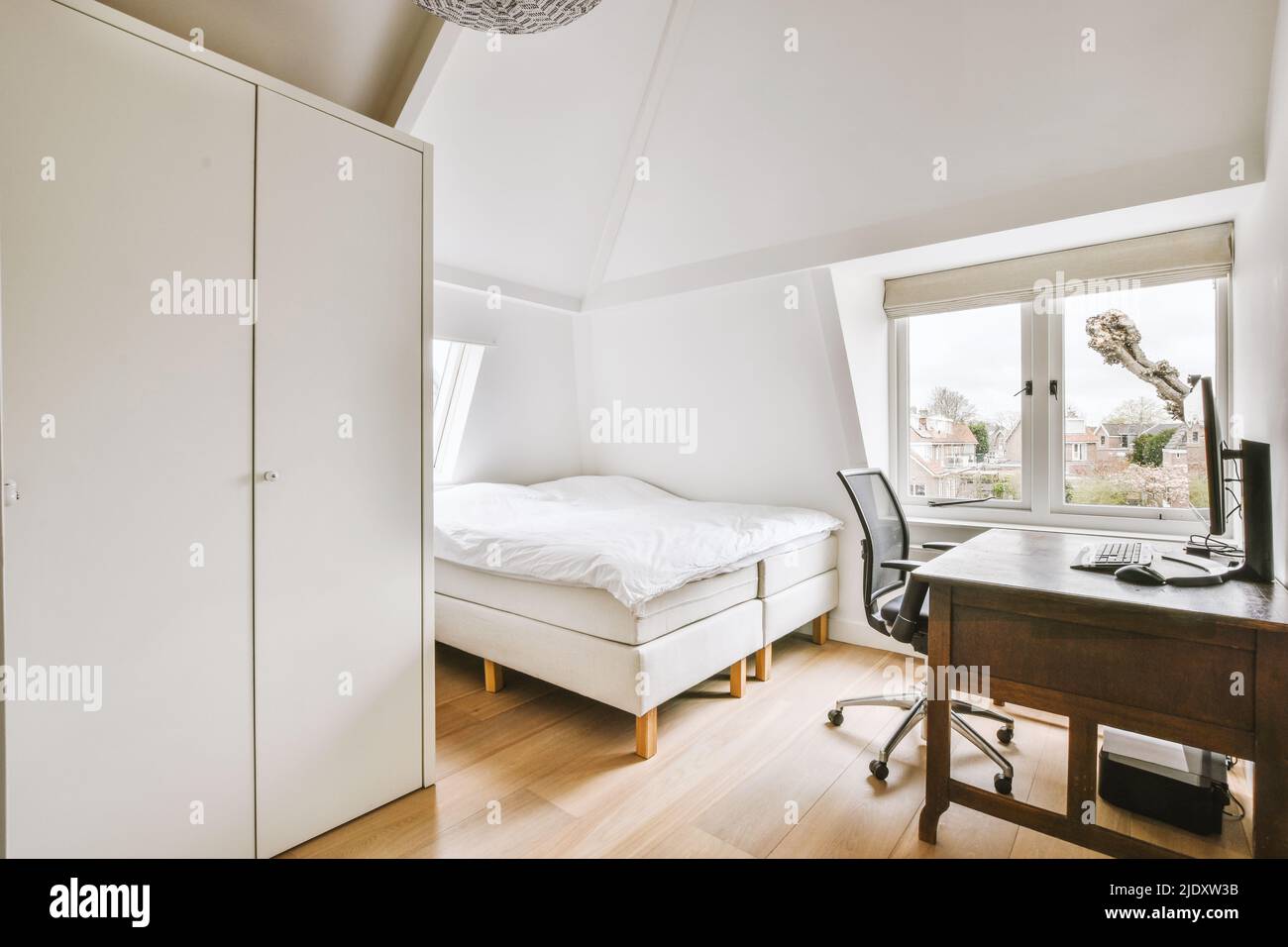 Comfortable bed opposite a computer desk with an armchair, in an attic ...