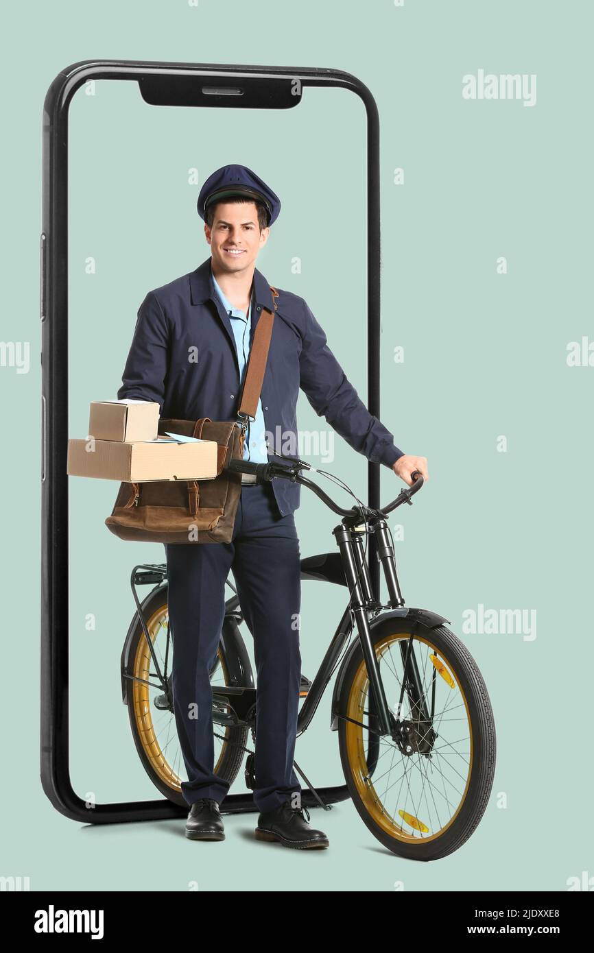 Young postman with bicycle and modern mobile phone on grey background ...