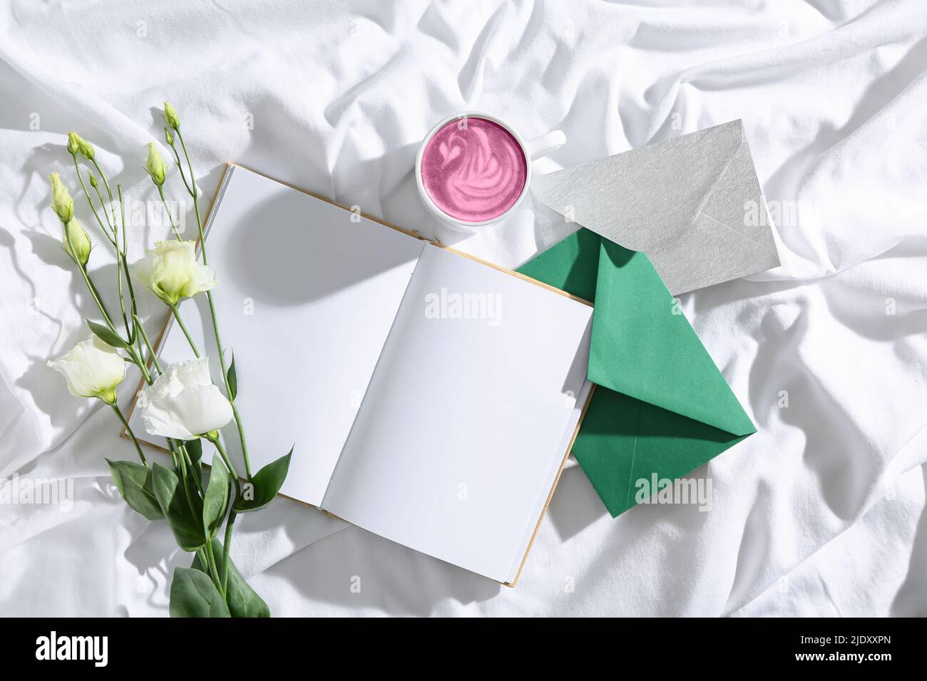 Cup of pink matcha tea with empty book, envelopes and flowers on bed ...