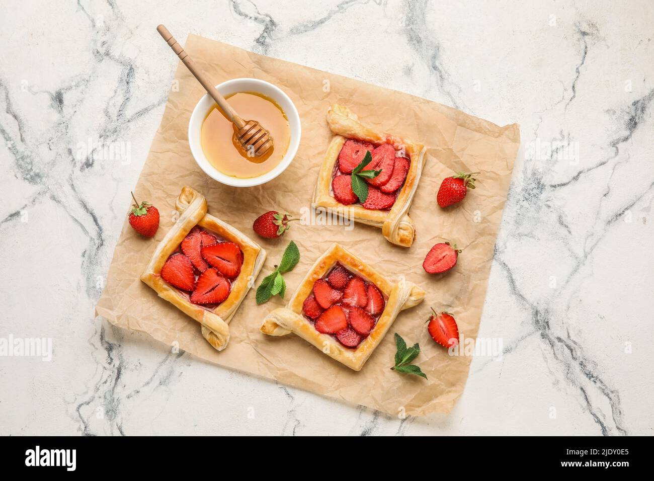 Delicious strawberry puff pastry and bowl with honey on white marble ...