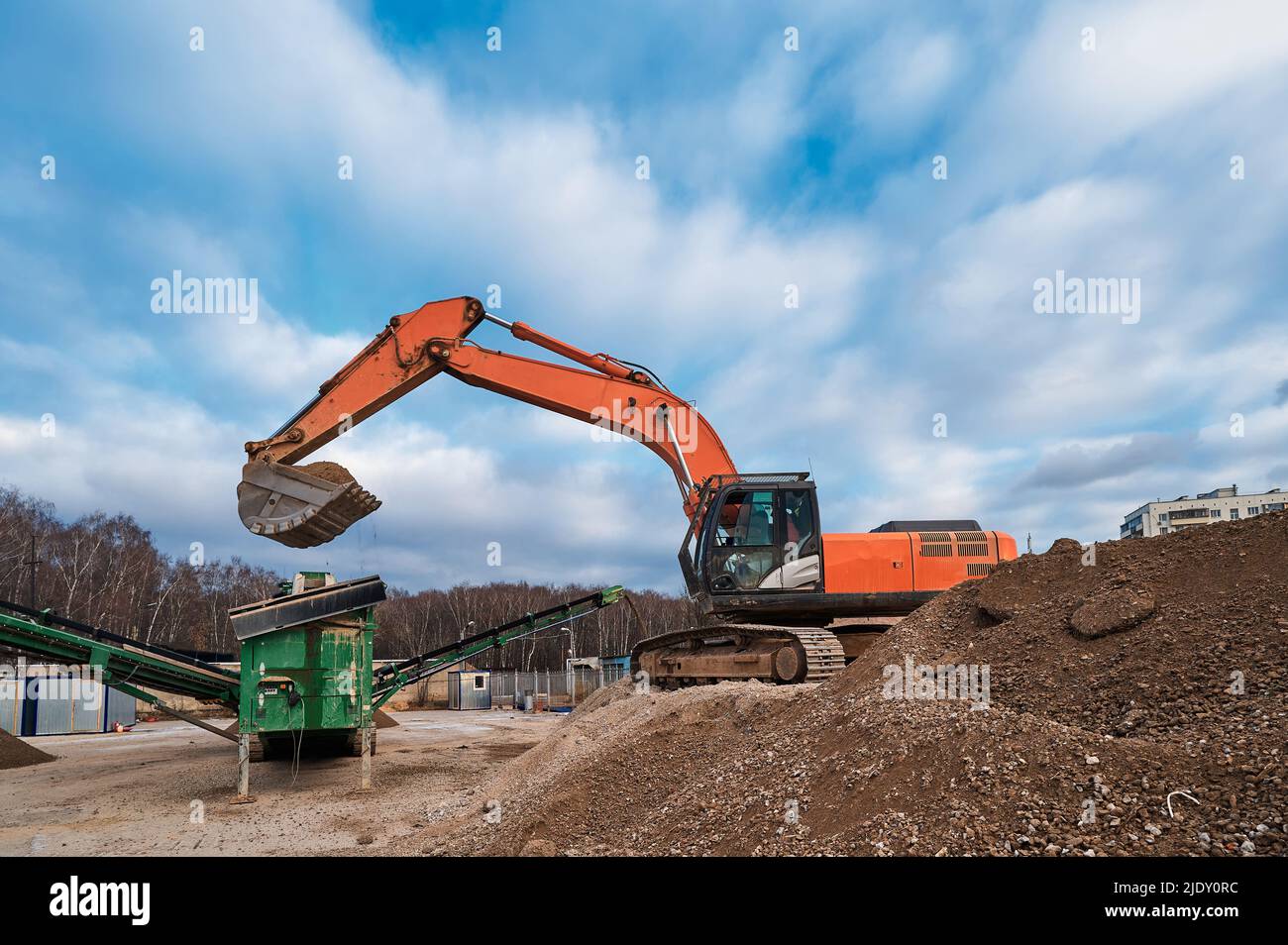A construction excavator loads crushed stone into the receiving hopper ...