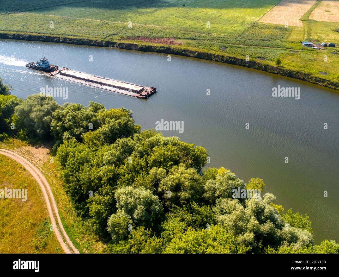 Small towboat pushes barge along calm water past fields Stock Photo - Alamy