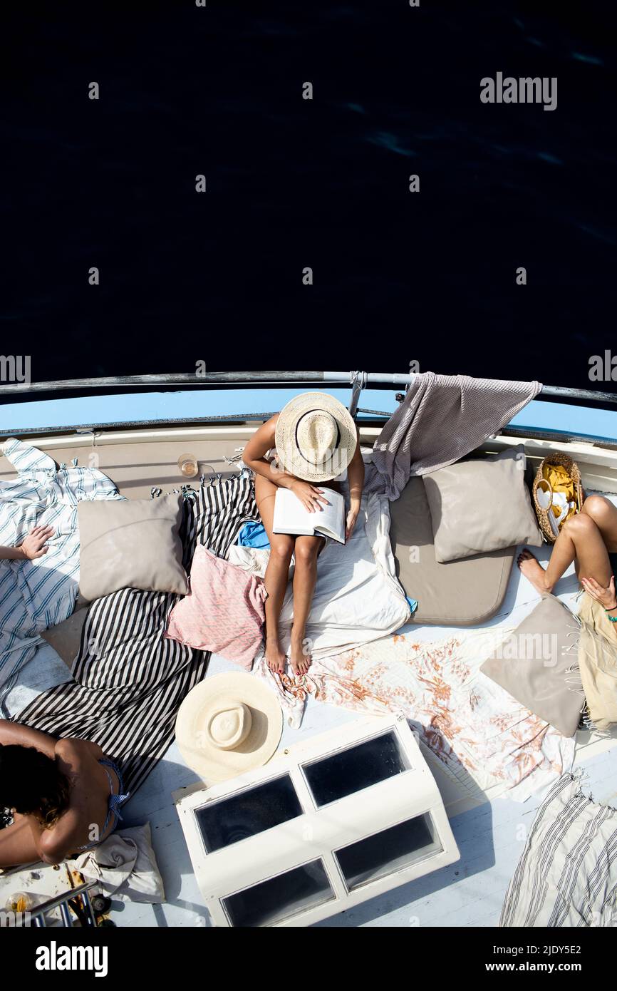 overhead of tan girl in bikini on a boat reading a book with hat on ...
