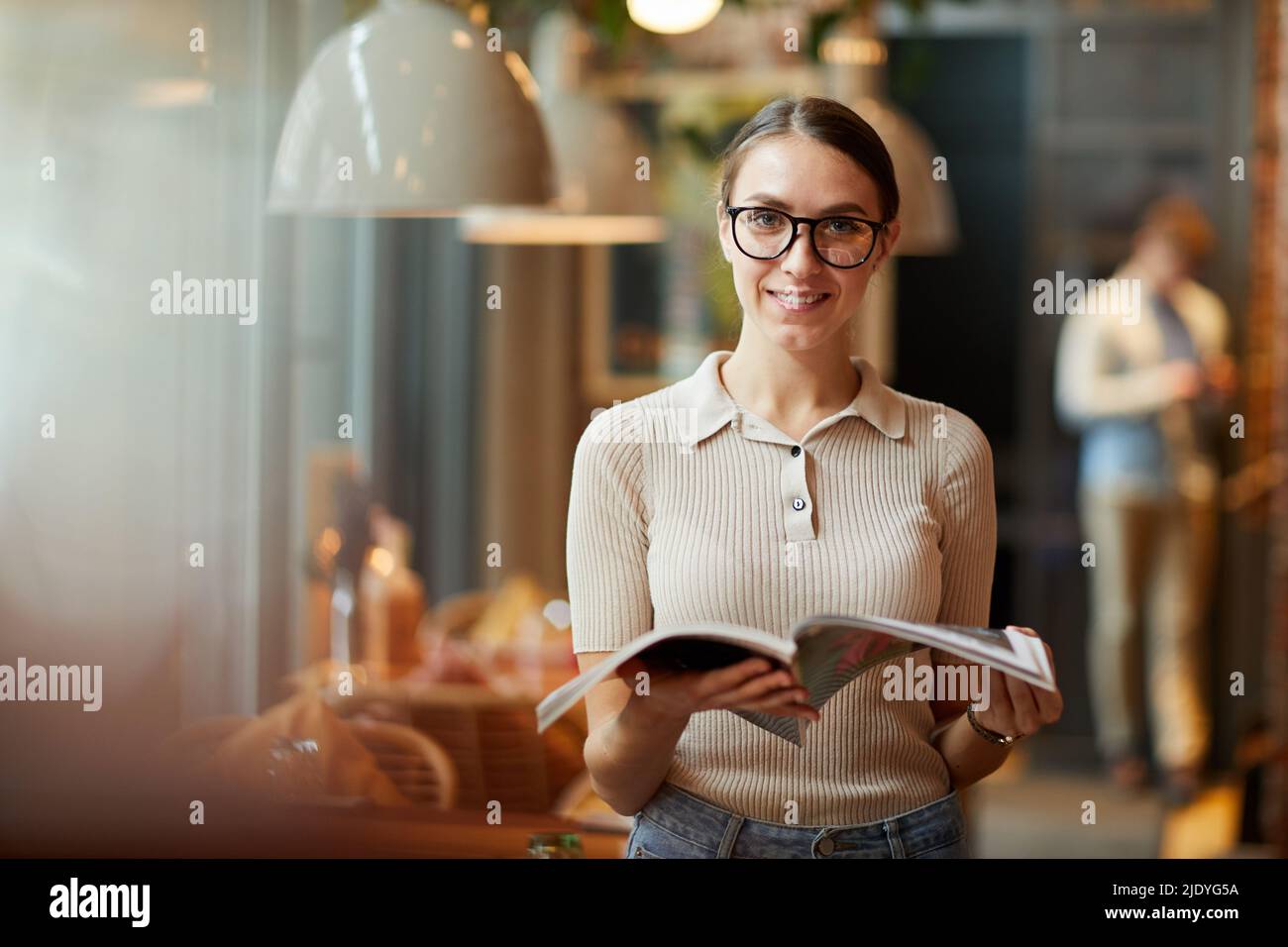 Portrait of cheerful beautiful female food critic in glasses holding ...