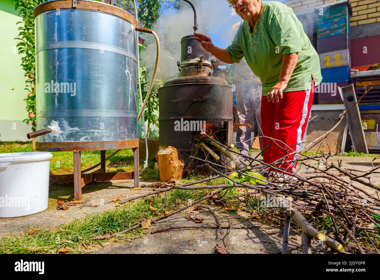Grandma throws dry branches into the firebox of a homemade distillery ...