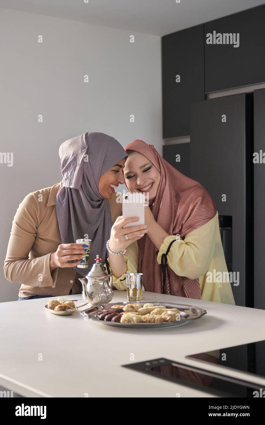 Two muslim women laugh and use the phone while having tea and arabic ...