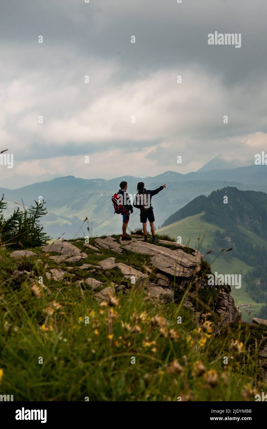 Two guys standing at the cliff of a mountain, one of them is pointing ...