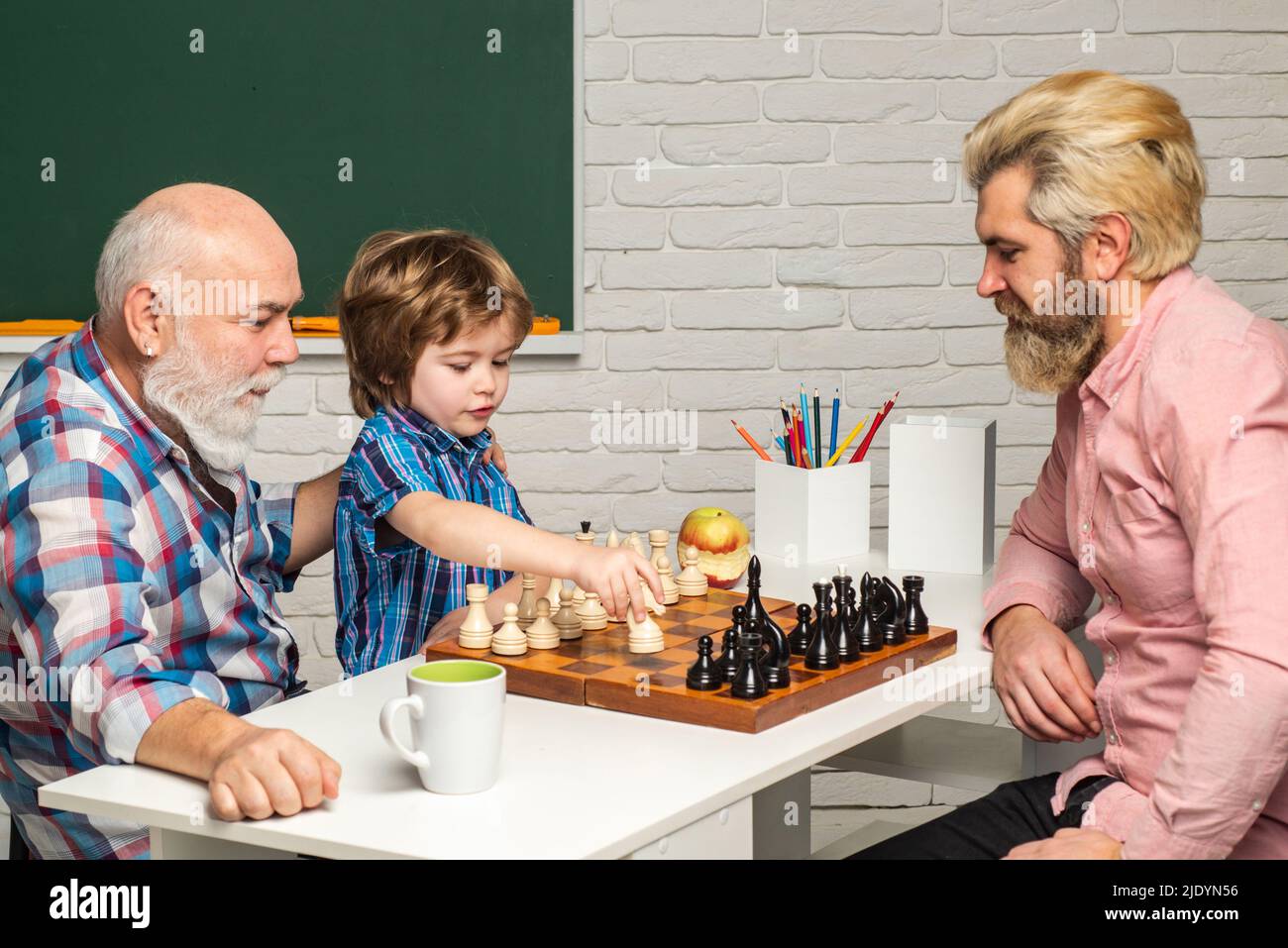 Grandfather father and son playing chess. Grandpa teaching grangson at ...