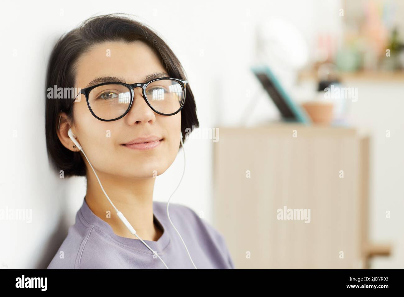 Portrait of smiling hipster girl in earphones and spectacles sitting by ...