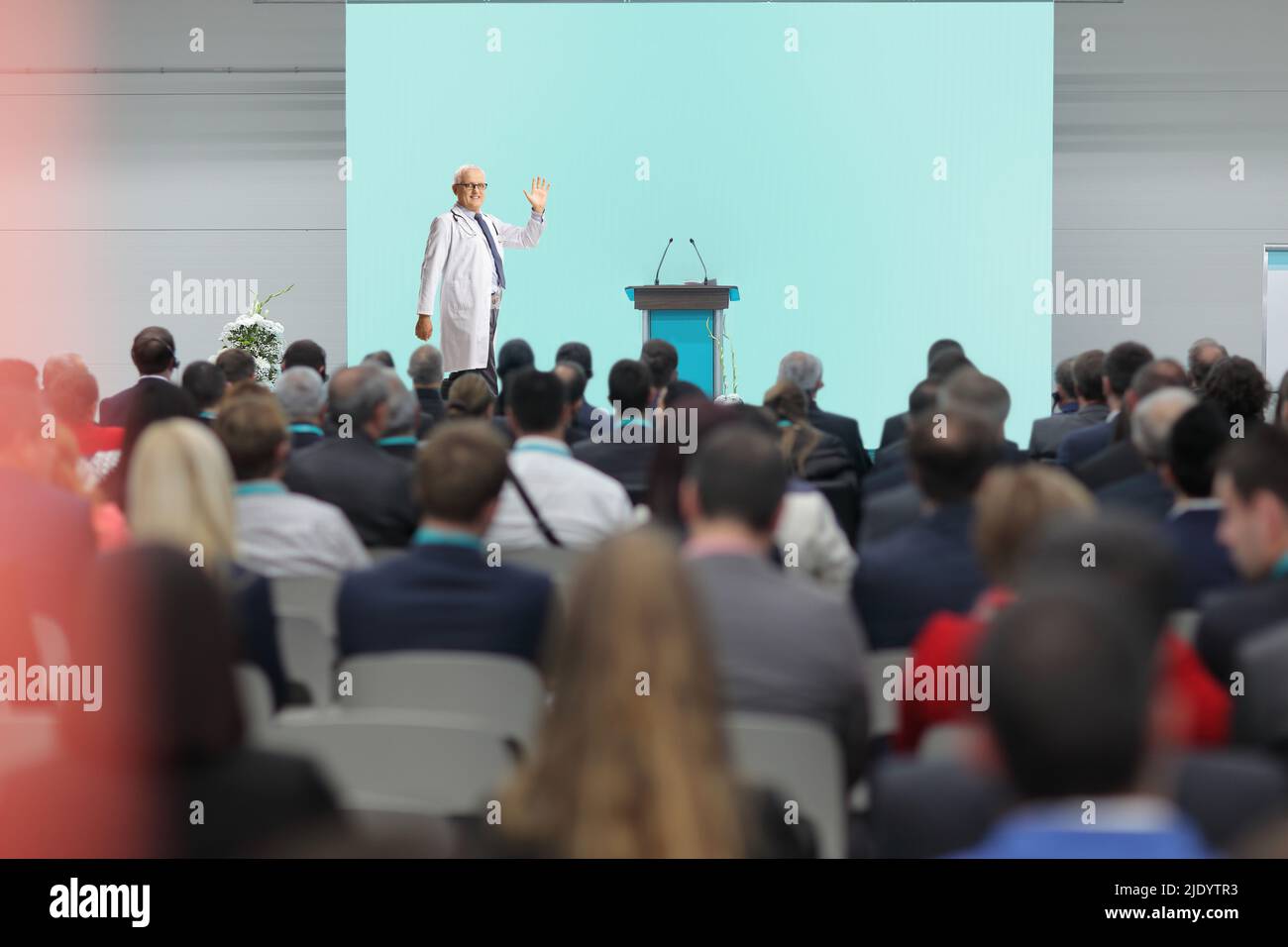 Male doctor waving at audience from the stage at a medical conference ...