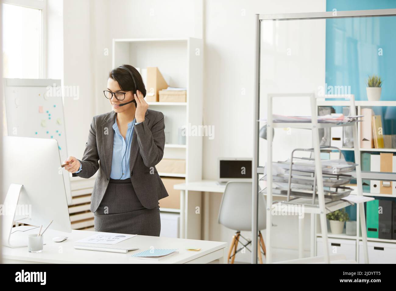 Content confident female manager in gray jacket standing at desk and ...